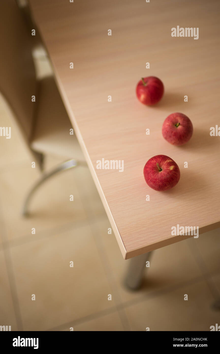 three red ripe apples on the wooden table in kitchen, room interior ...
