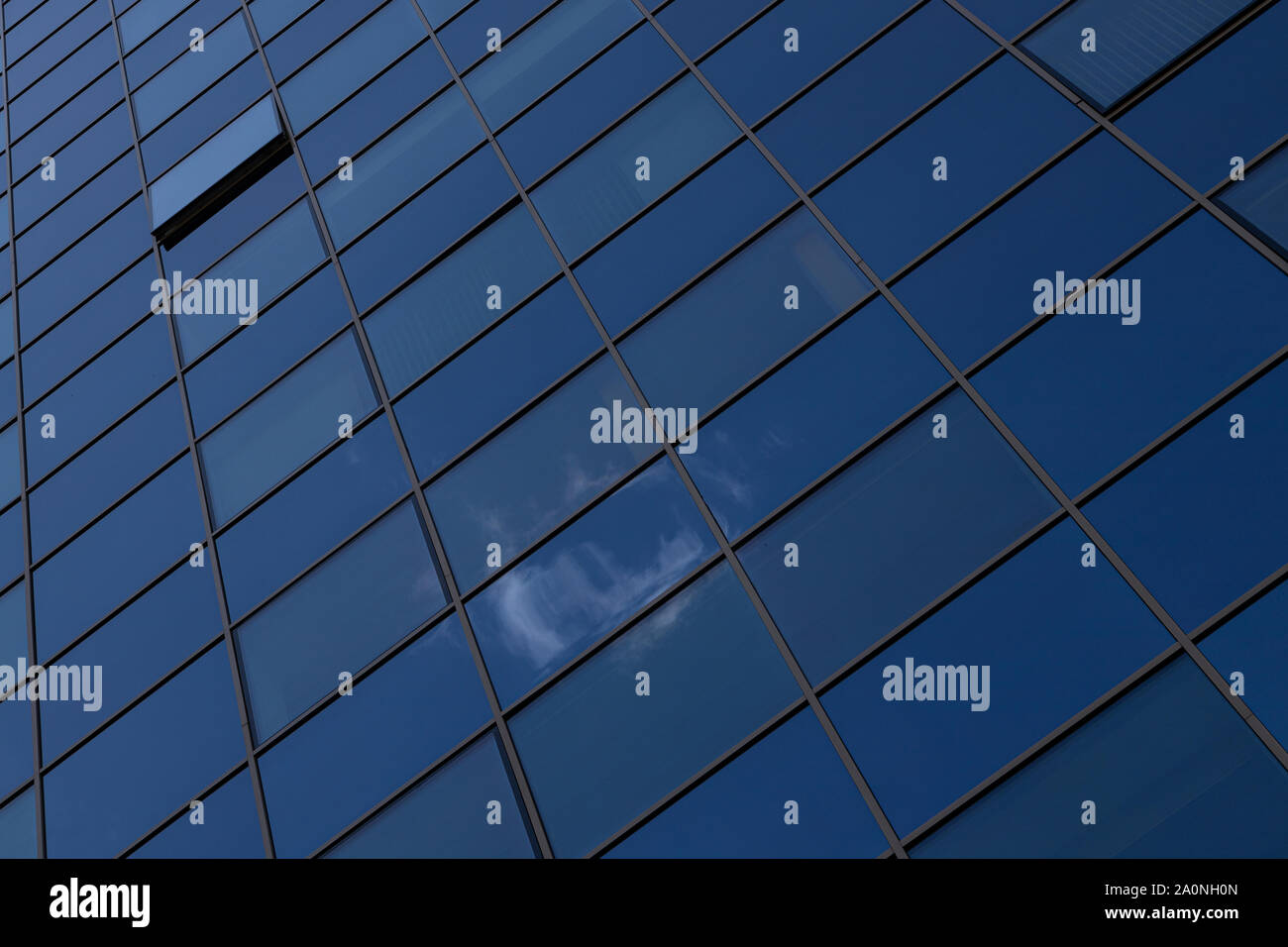 Ground view of blue glass surface of building wall reflecting blue sky ...