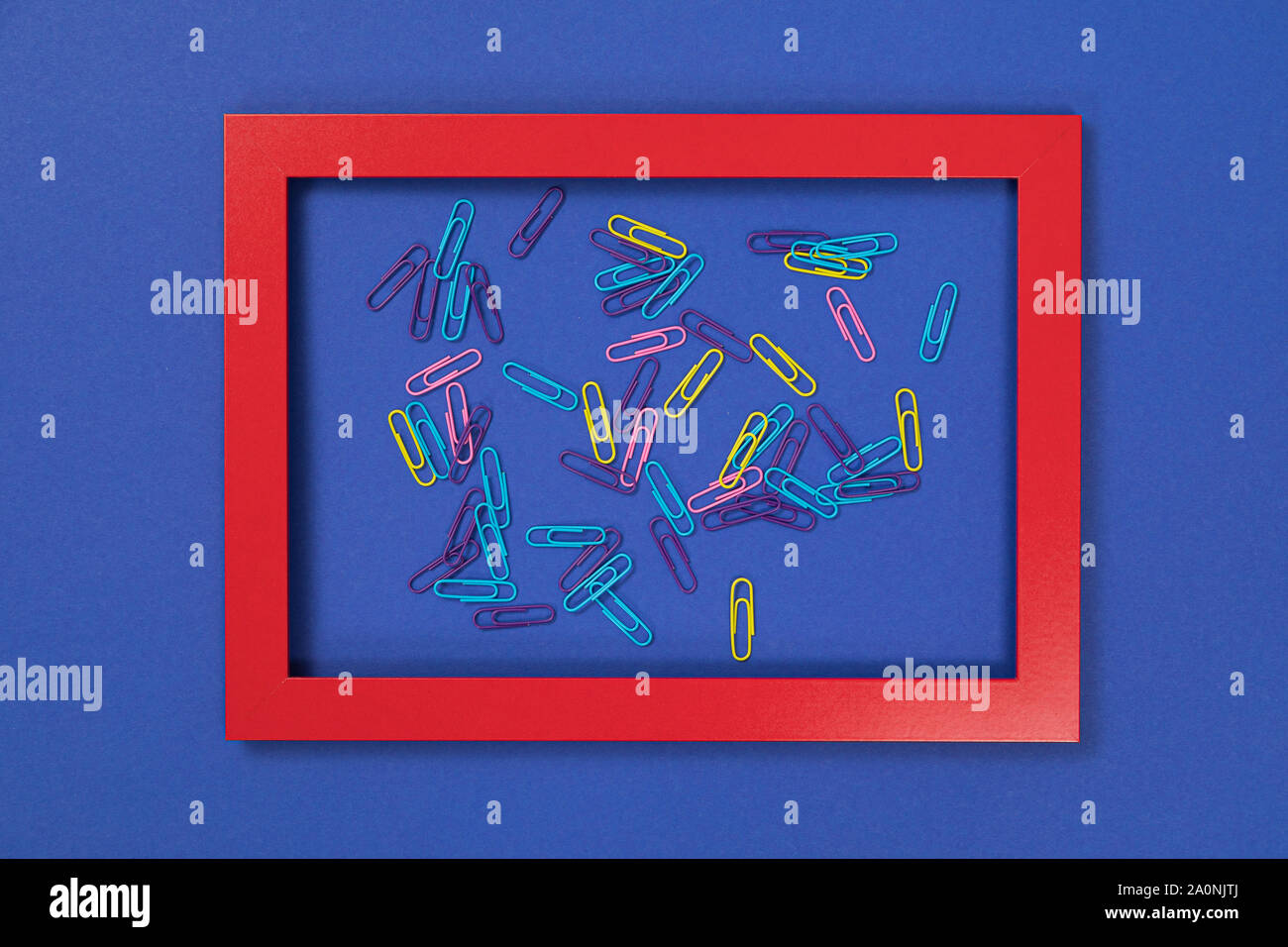 A group of colorful paper fasteners scattered in a red frame on blue ...