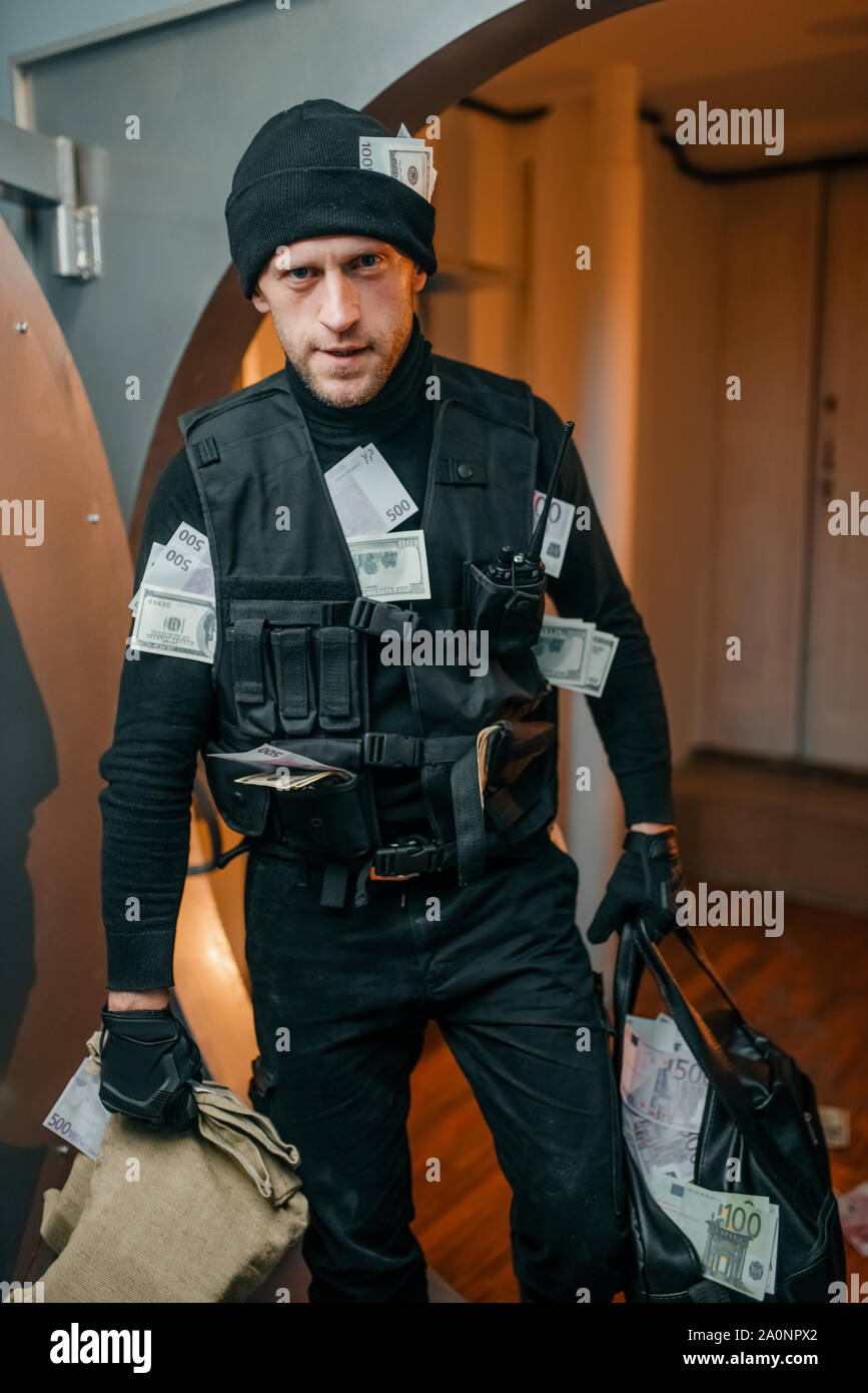 Robber in black uniform holds bags full of money Stock Photo - Alamy