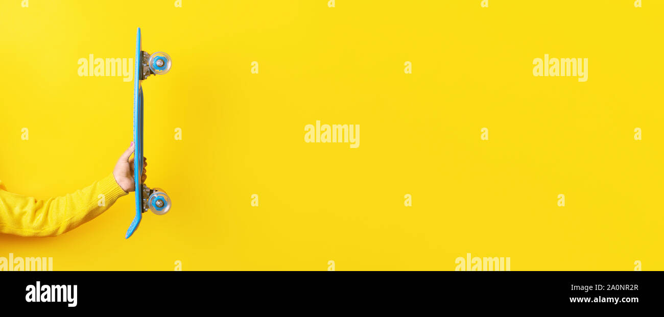 hand holding blue skate board over yellow background, panoramic mock up ...