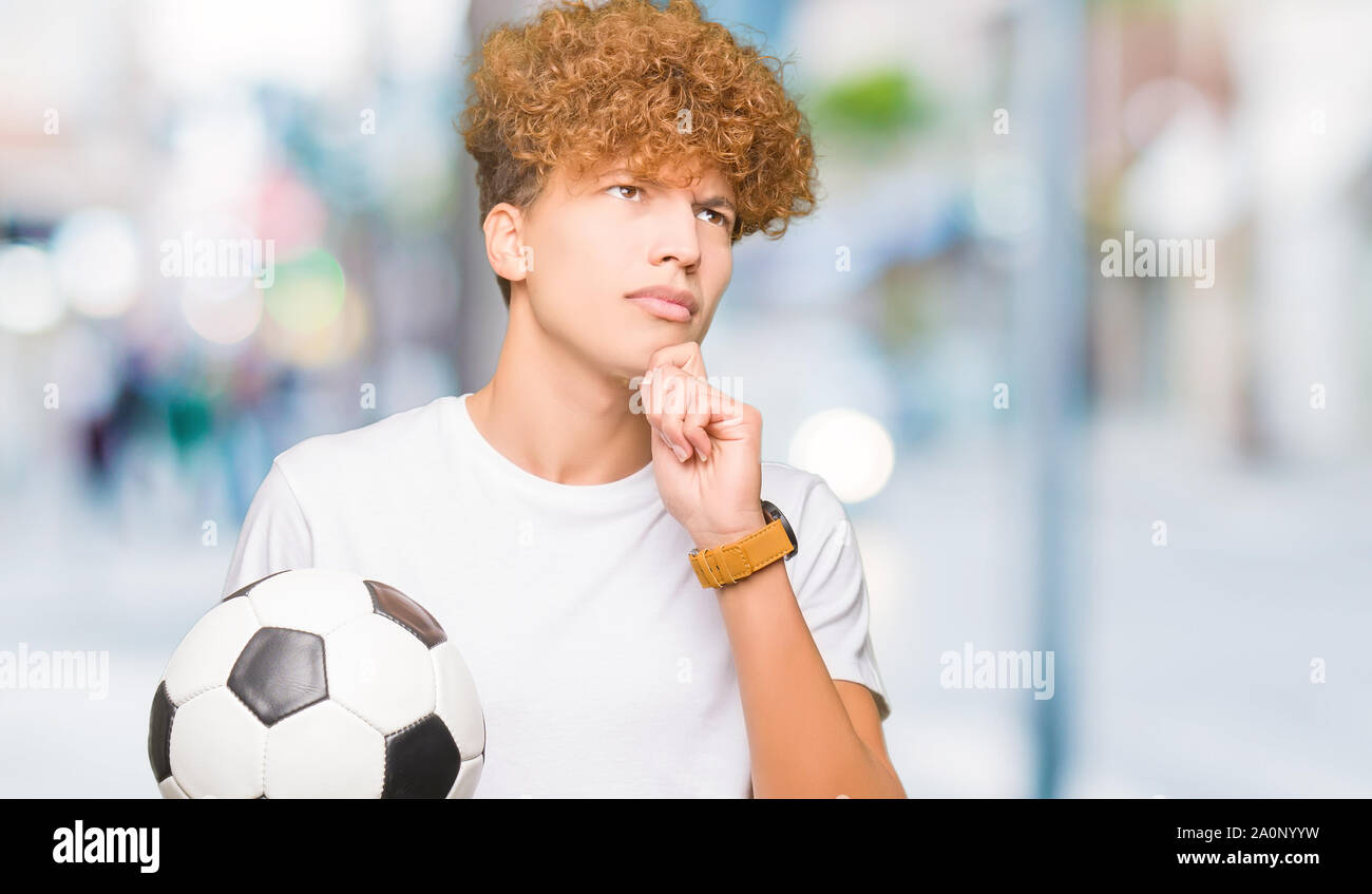 Young handsome man holding soccer football ball serious face thinking ...