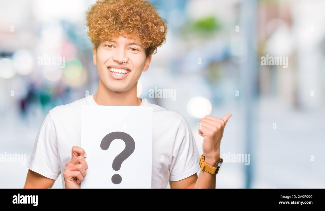 Young handsome man holding paper with question mark pointing and ...