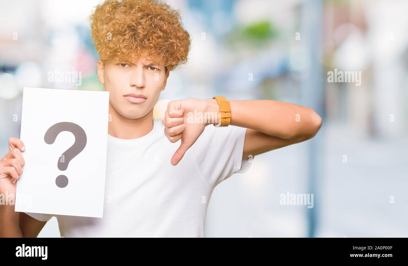 Young handsome man holding paper with question mark with angry face ...