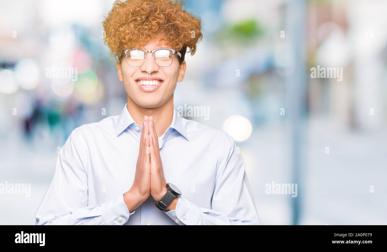 Young handsome business man with afro wearing glasses praying with ...