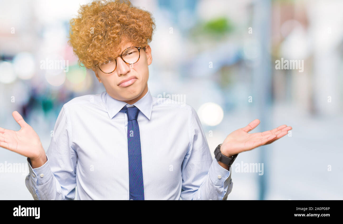 Young handsome business man with afro wearing glasses clueless and ...