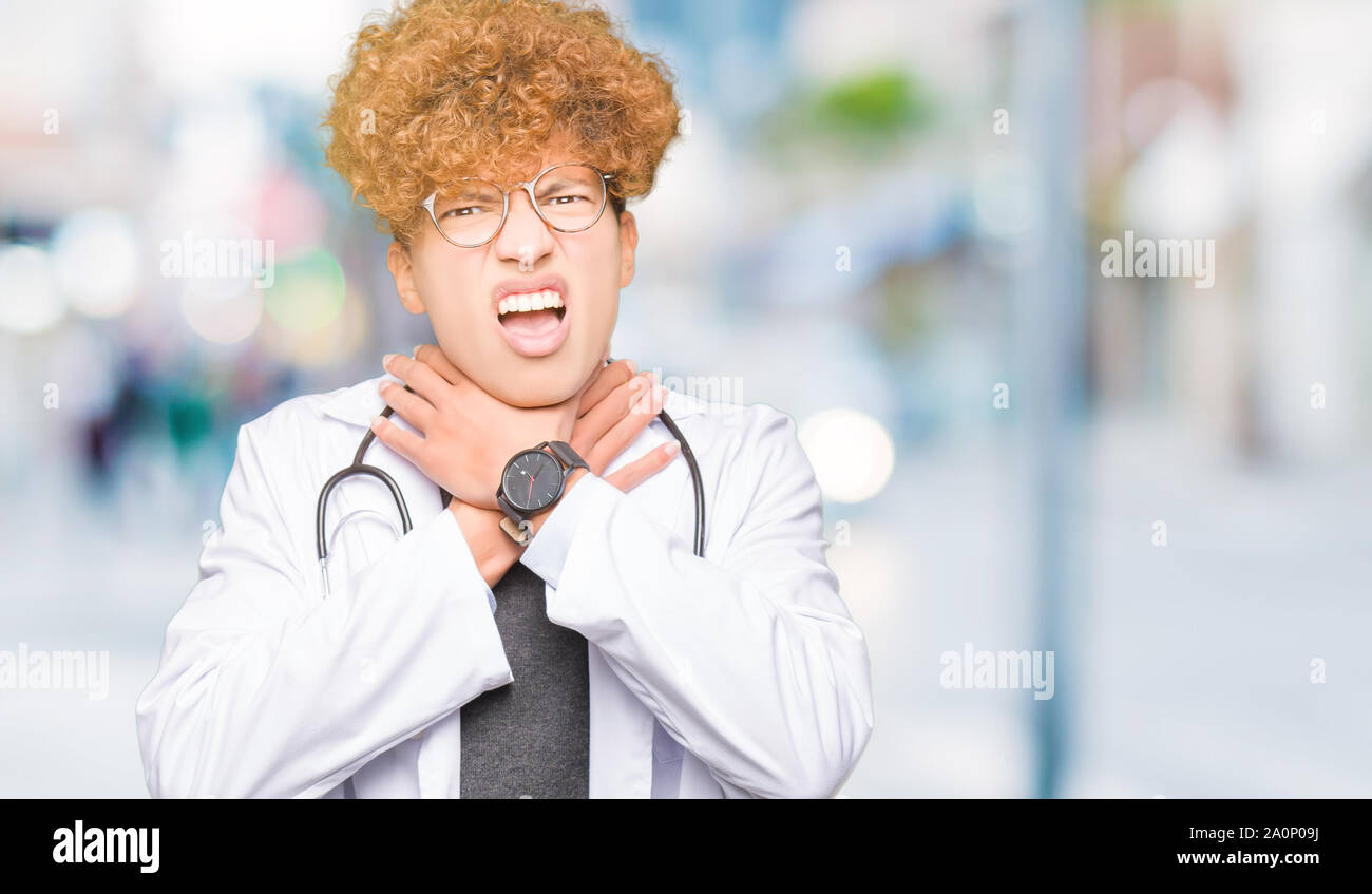 Young handsome doctor man wearing medical coat shouting and suffocate ...