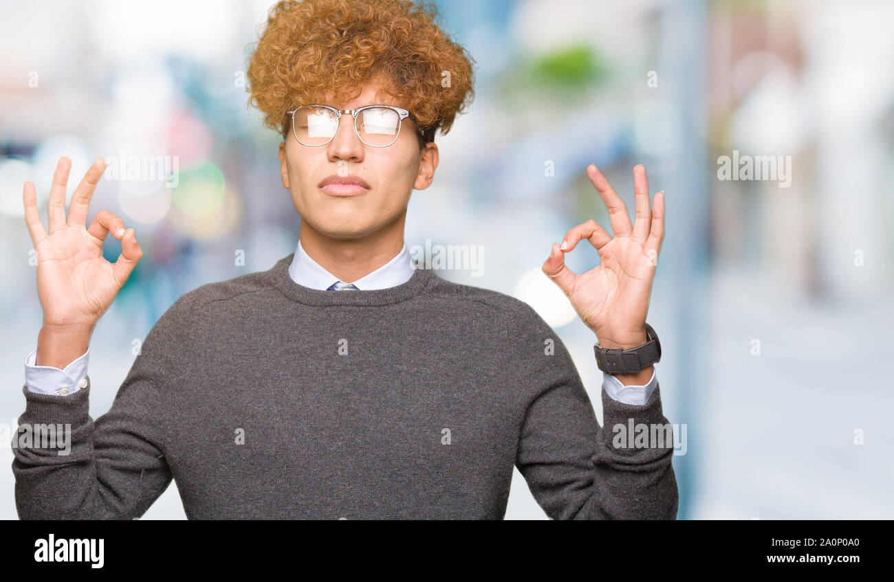 Young handsome business man with afro hair wearing glasses relax and ...