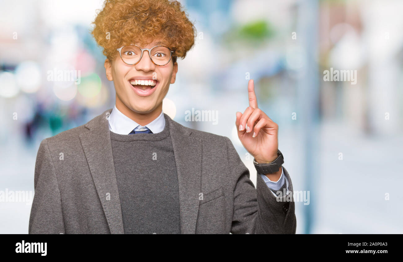 Young handsome business man with afro wearing glasses pointing finger ...
