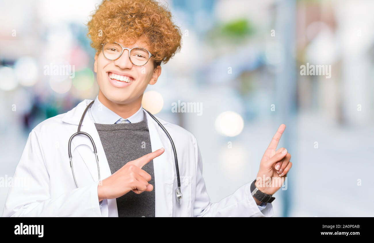 Young handsome doctor man wearing medical coat smiling and looking at ...