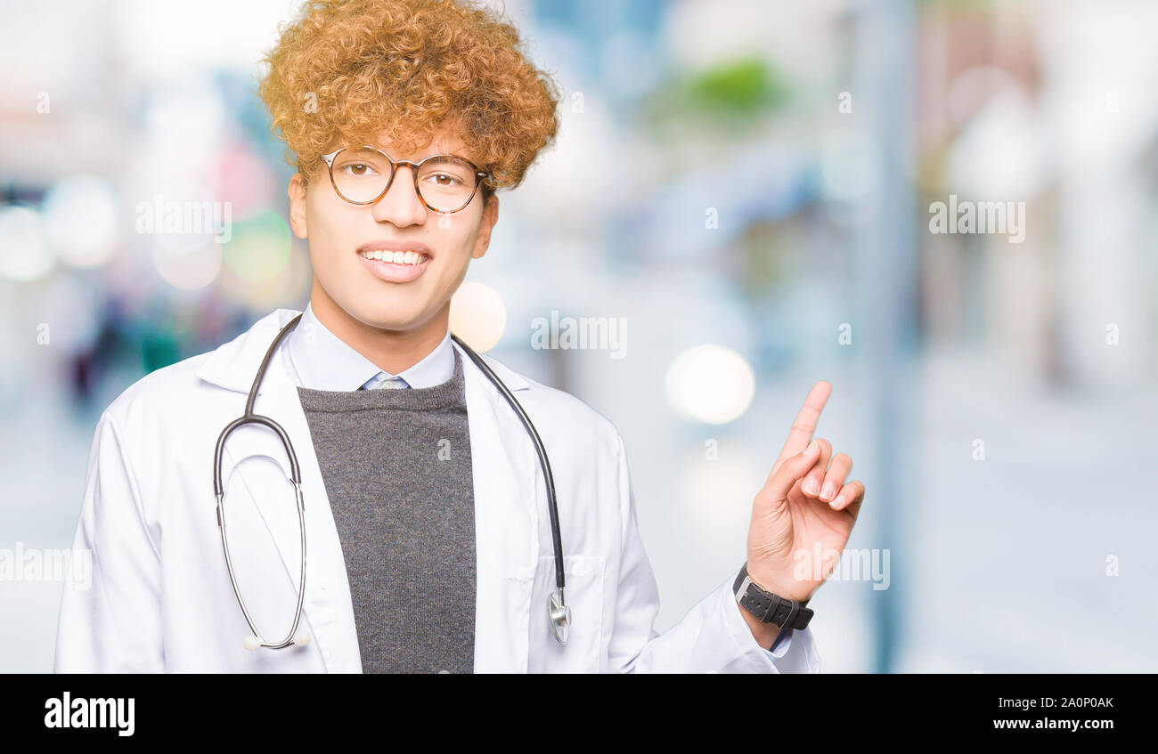Young handsome doctor man wearing medical coat with a big smile on face ...