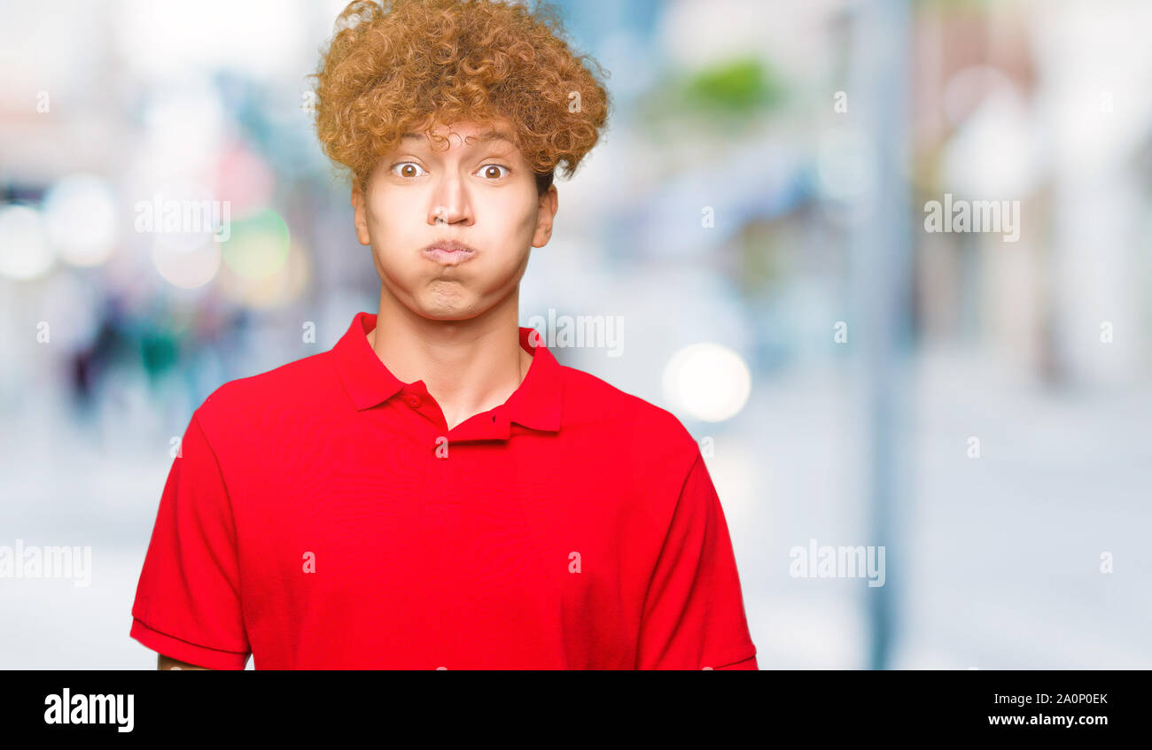 Young handsome man with afro hair wearing red t-shirt puffing cheeks ...