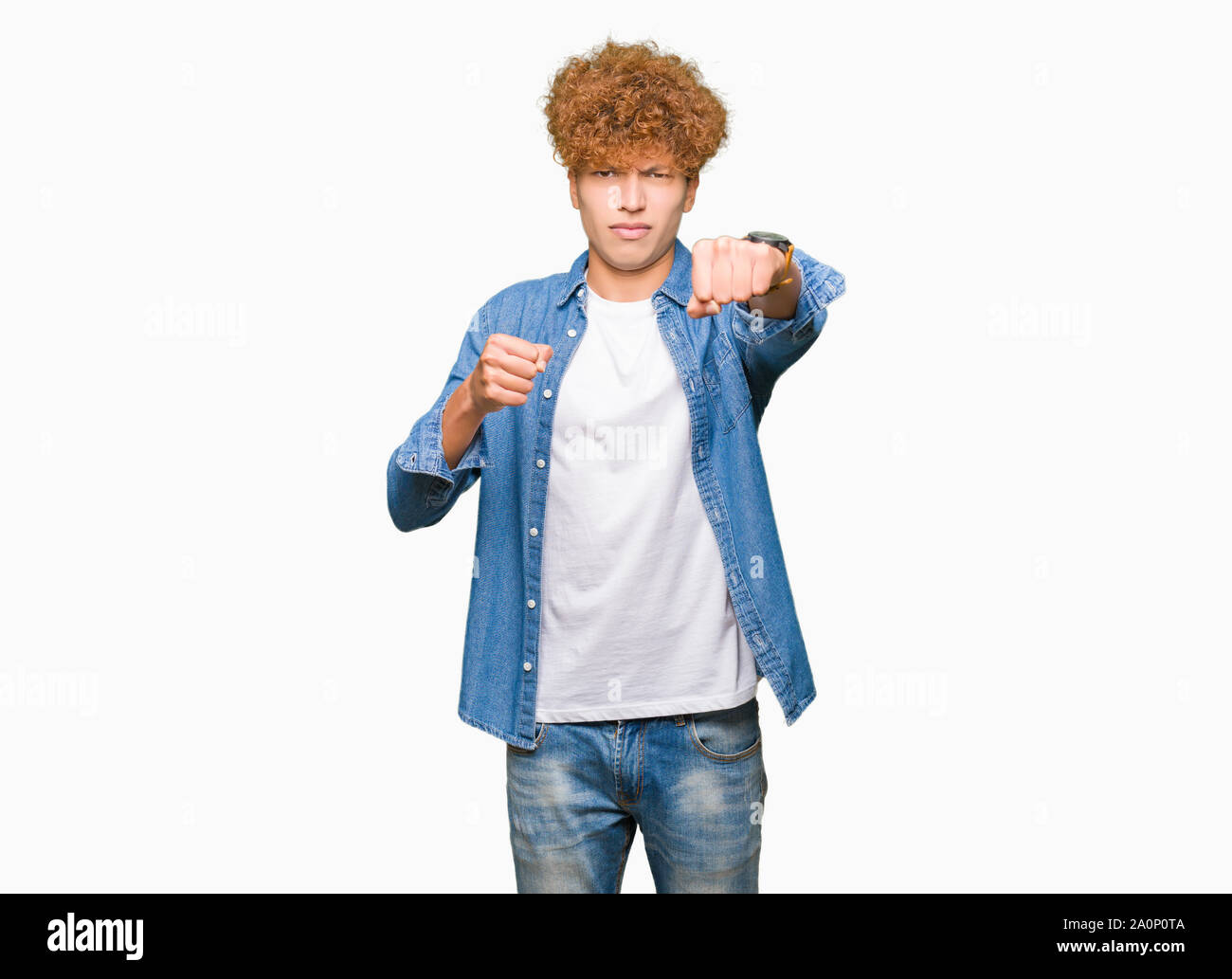 Young handsome man with afro hair wearing denim jacket Punching fist to ...