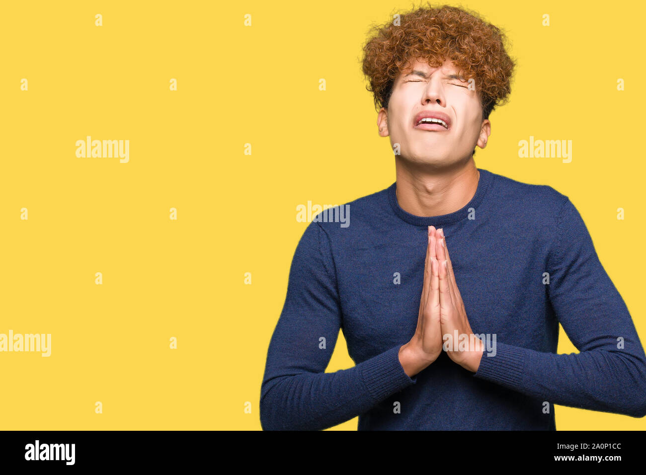 Young handsome man with afro hair begging and praying with hands ...