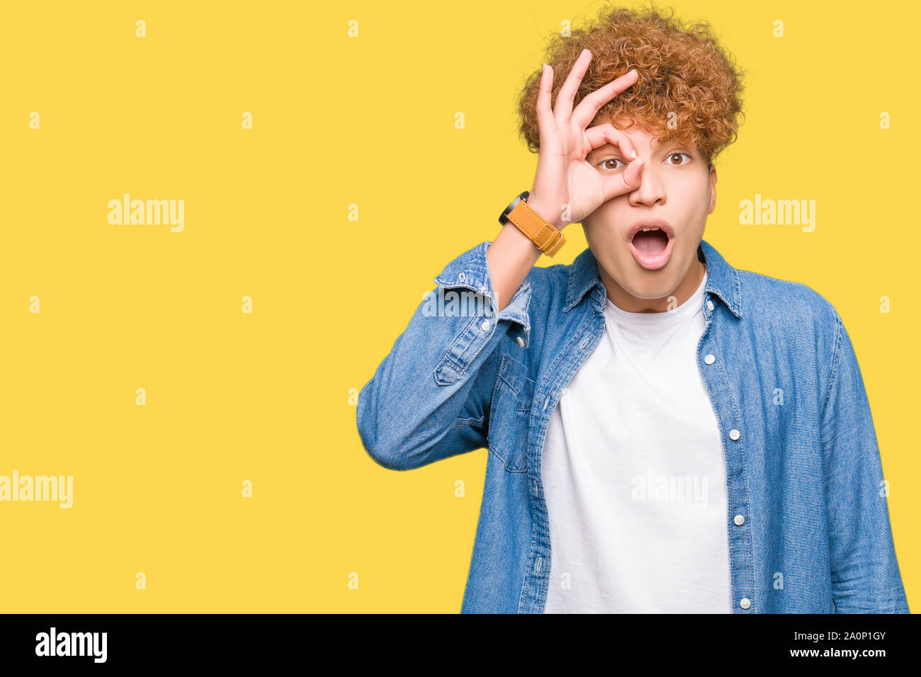 Young handsome man with afro hair wearing denim jacket doing ok gesture ...