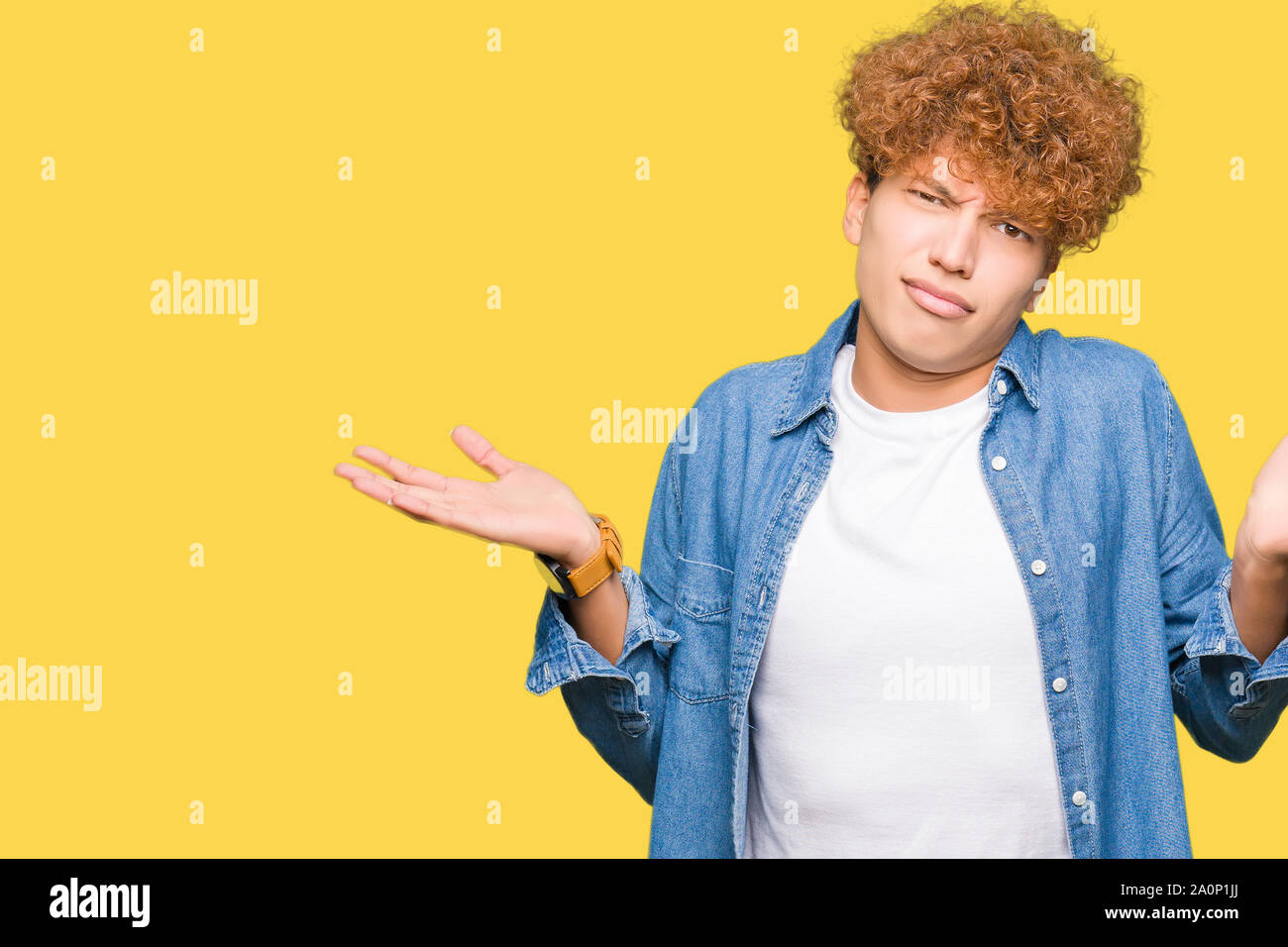 Young handsome man with afro hair wearing denim jacket clueless and ...