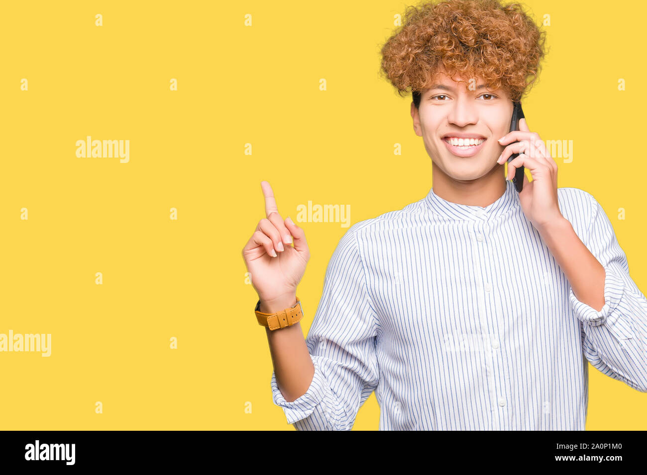 Young handsome man talking on the phone very happy pointing with hand ...