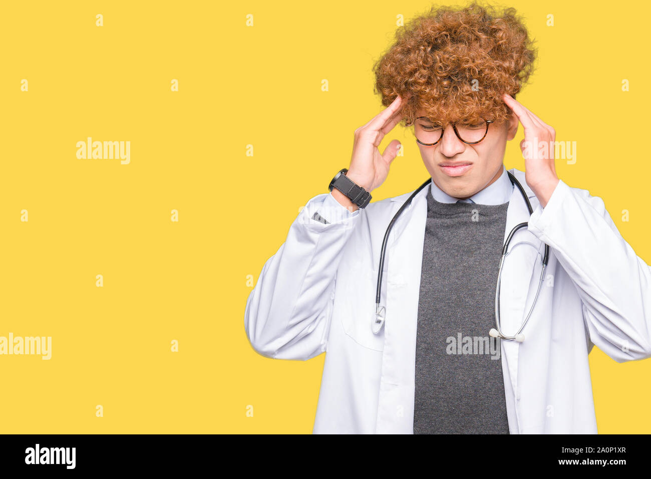 Young handsome doctor man wearing medical coat with hand on head for ...
