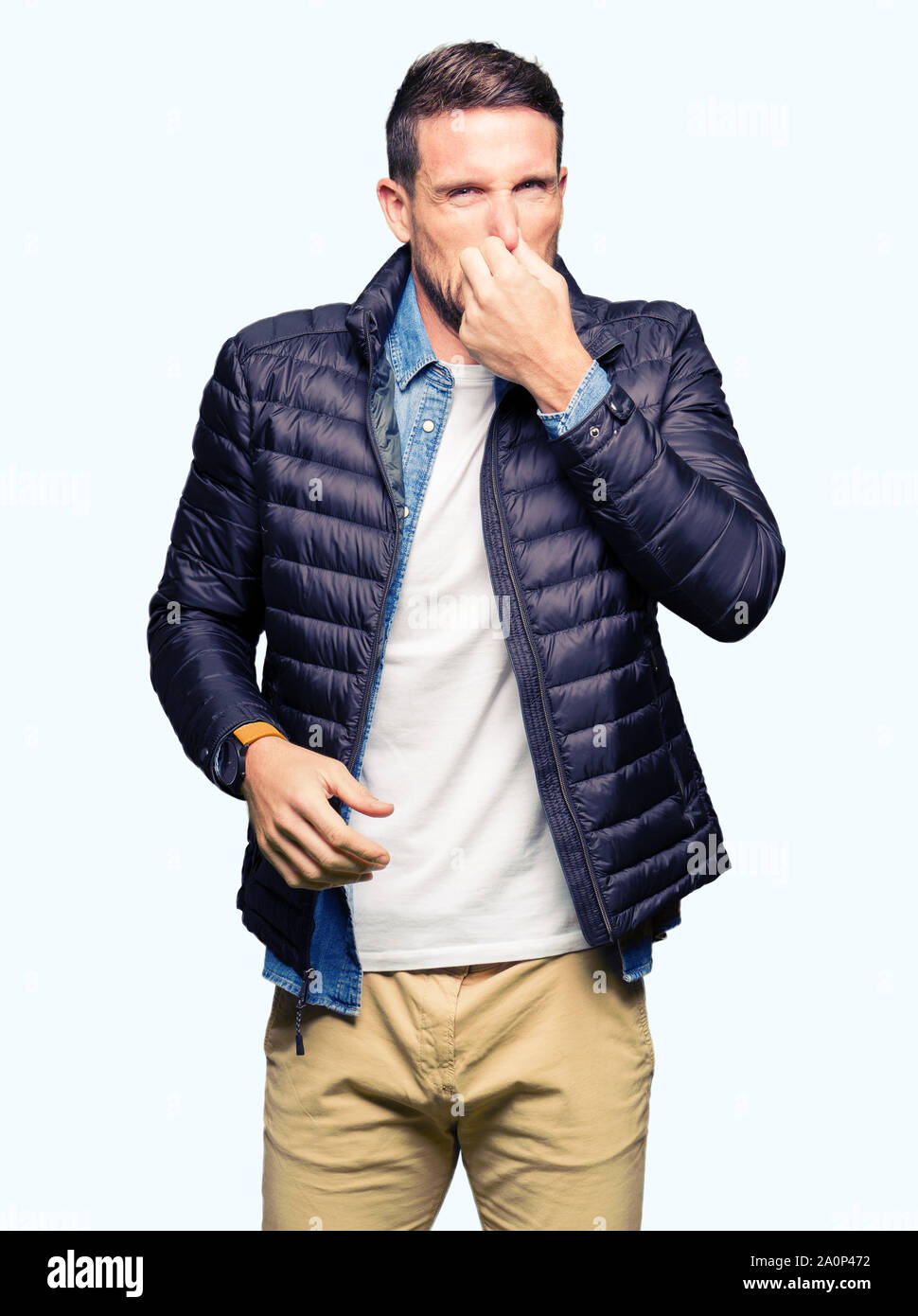 Handsome man wearing winter coat smelling something stinky and ...
