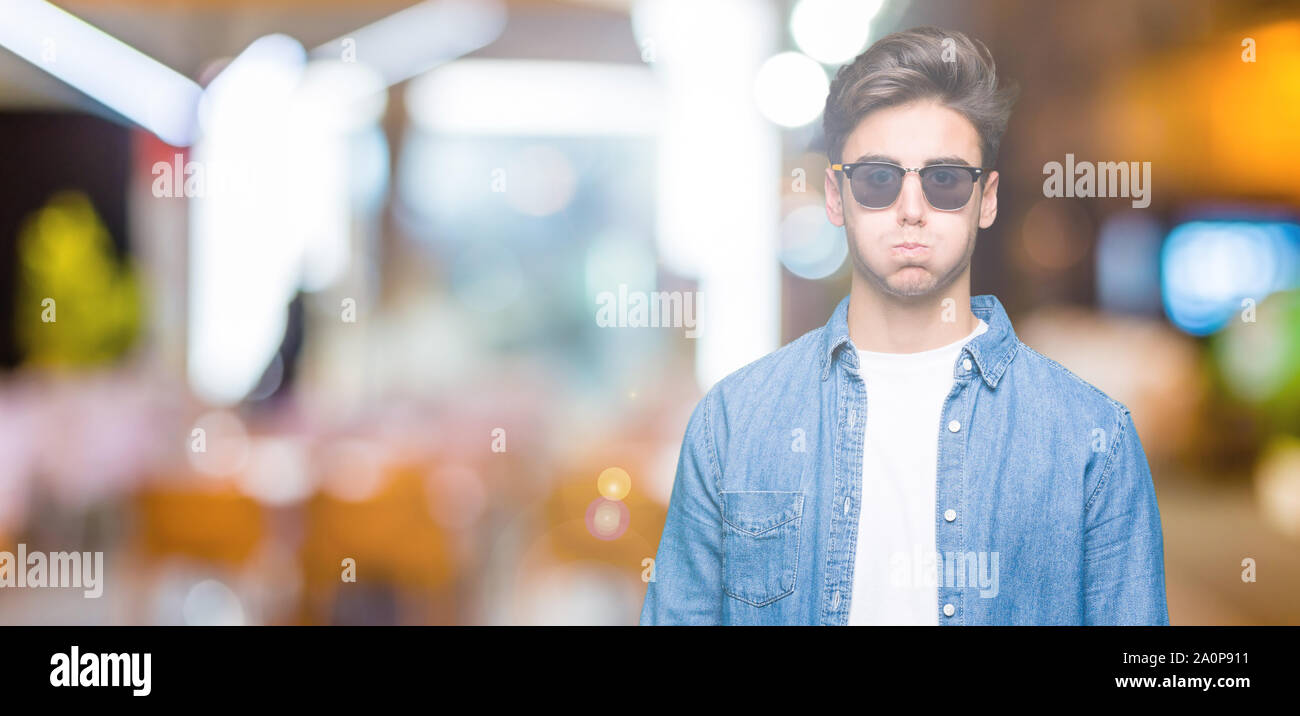Young handsome man wearing sunglasses over isolated background puffing ...