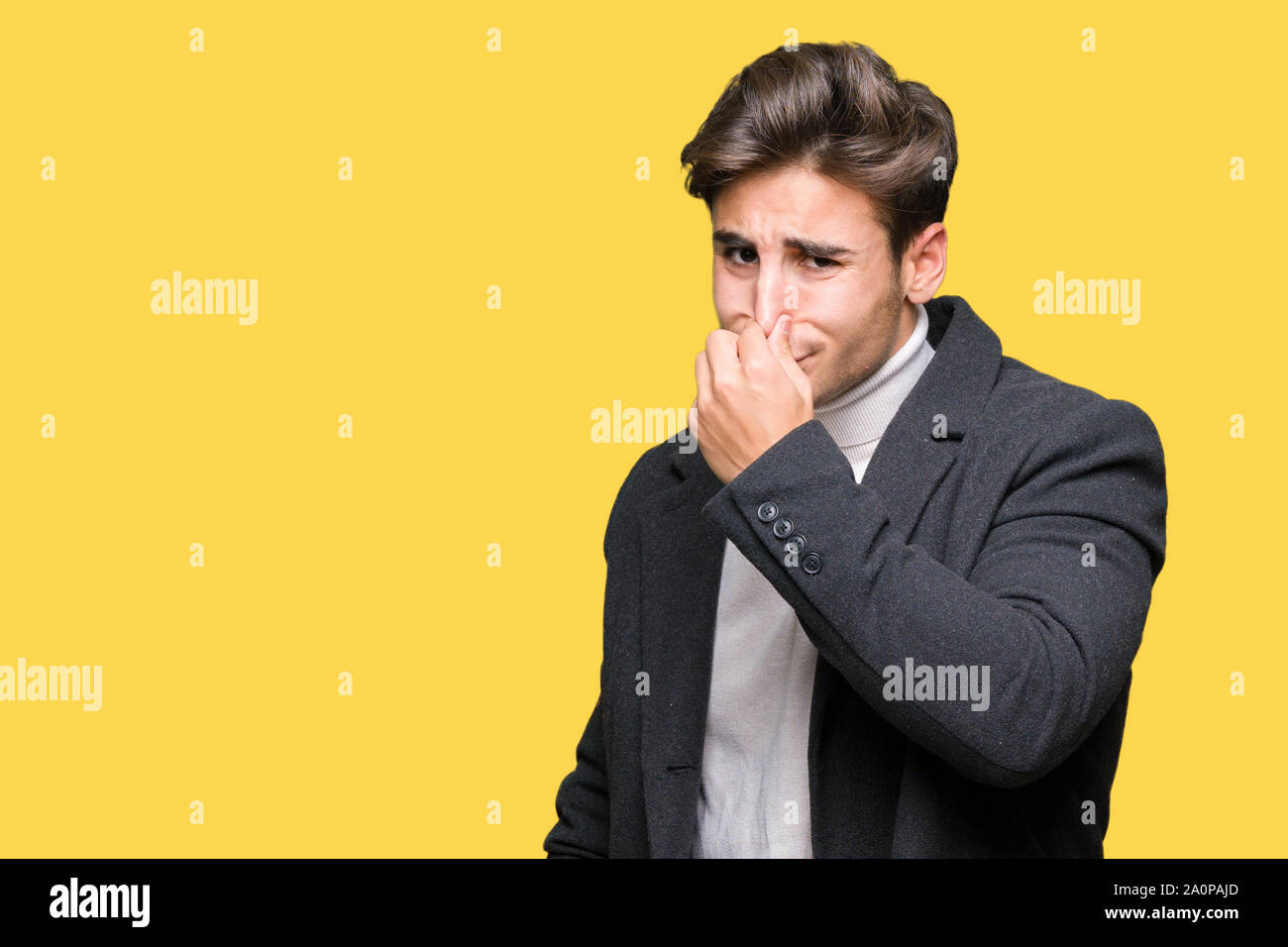 Young elegant man wearing winter coat over isolated background smelling ...