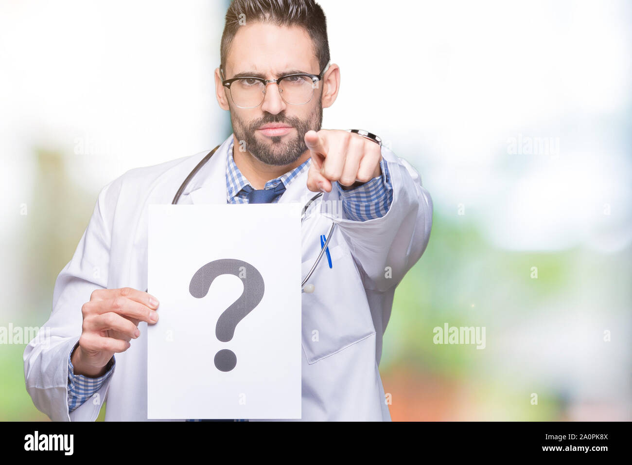 Handsome young doctor man holding paper with question mark over ...