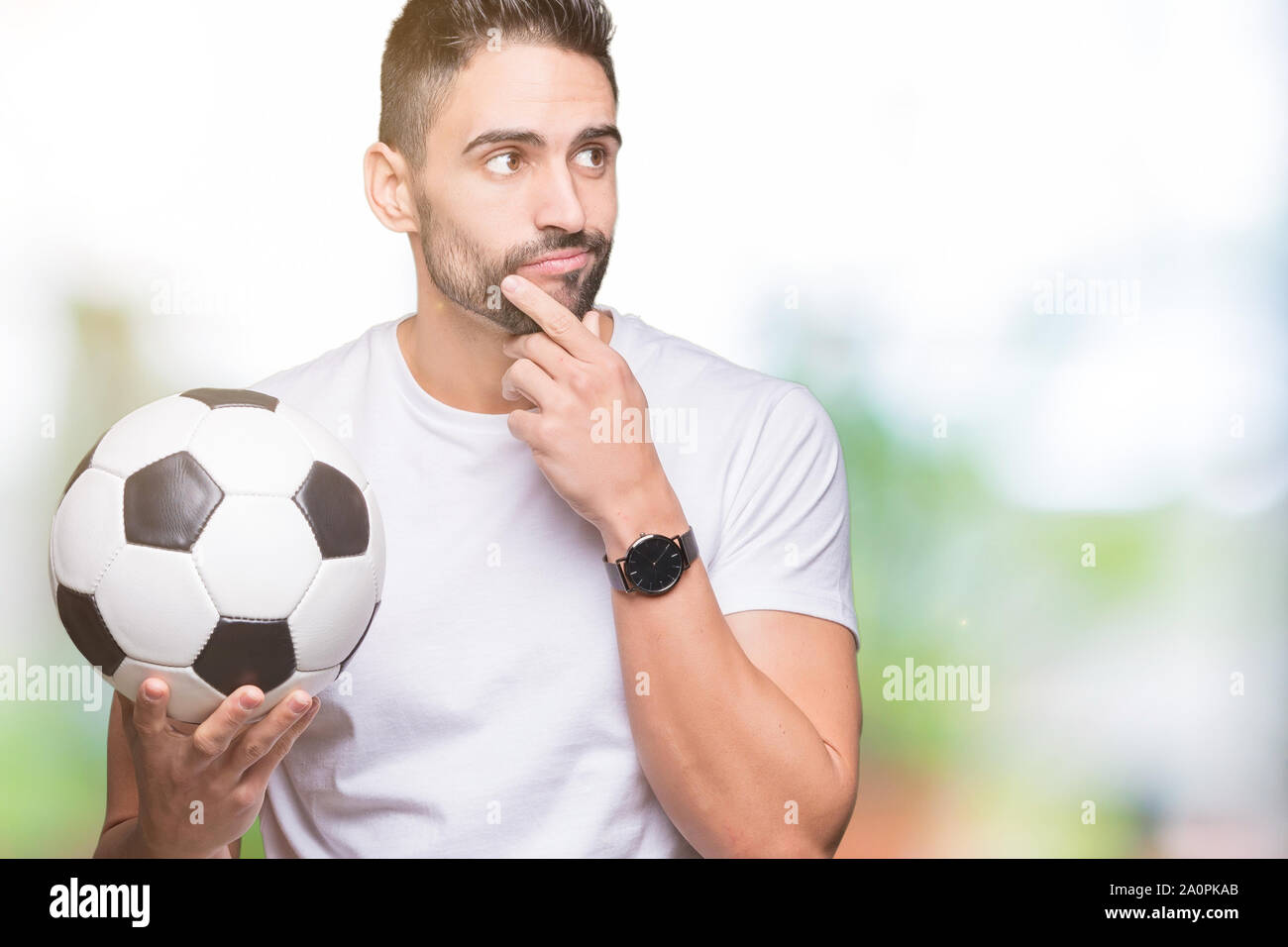 Young man holding soccer football ball over isolated background serious ...