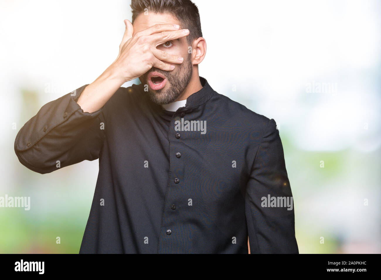 Young Christian priest over isolated background peeking in shock ...