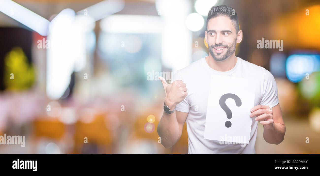 Handsome young man holding paper with question mark over isolated ...