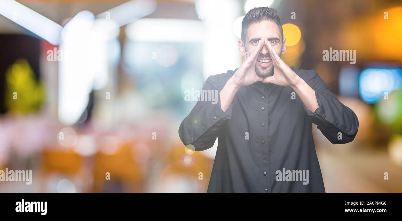 Young Christian priest over isolated background Shouting angry out loud ...