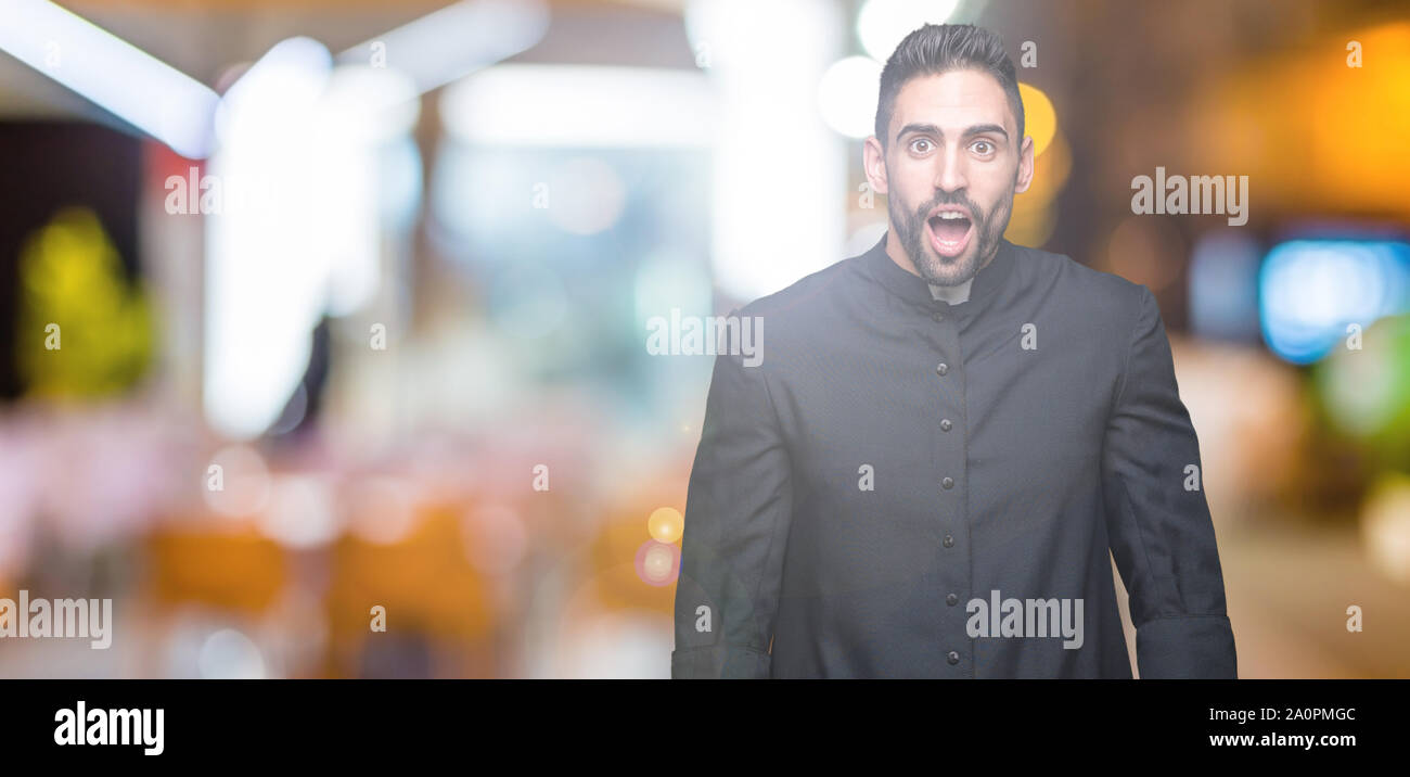 Young Christian priest over isolated background In shock face, looking ...