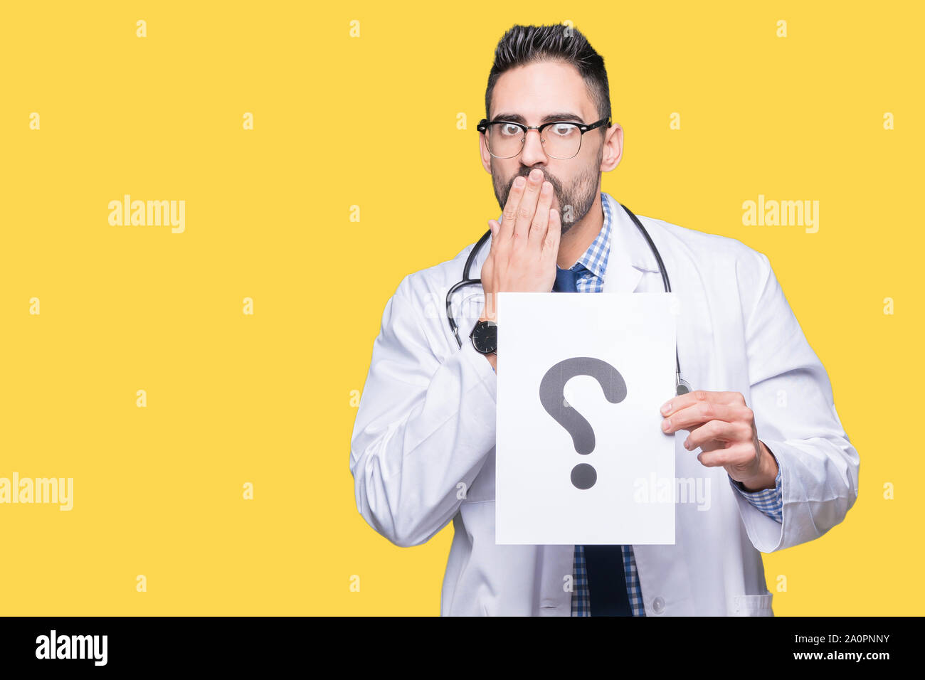 Handsome young doctor man holding paper with question mark over ...