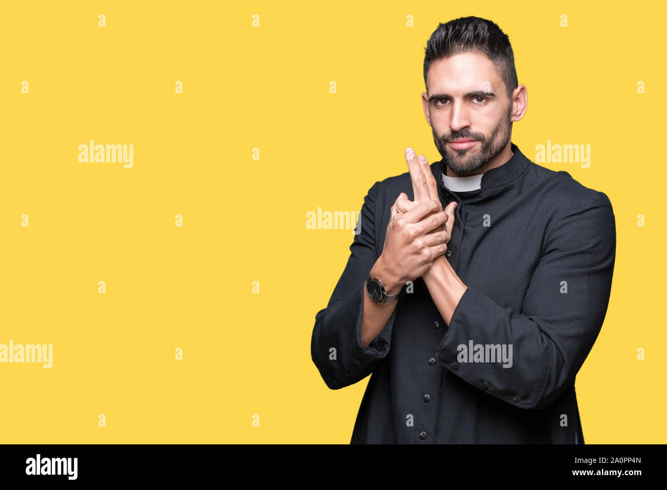 Young Christian priest over isolated background Holding symbolic gun ...