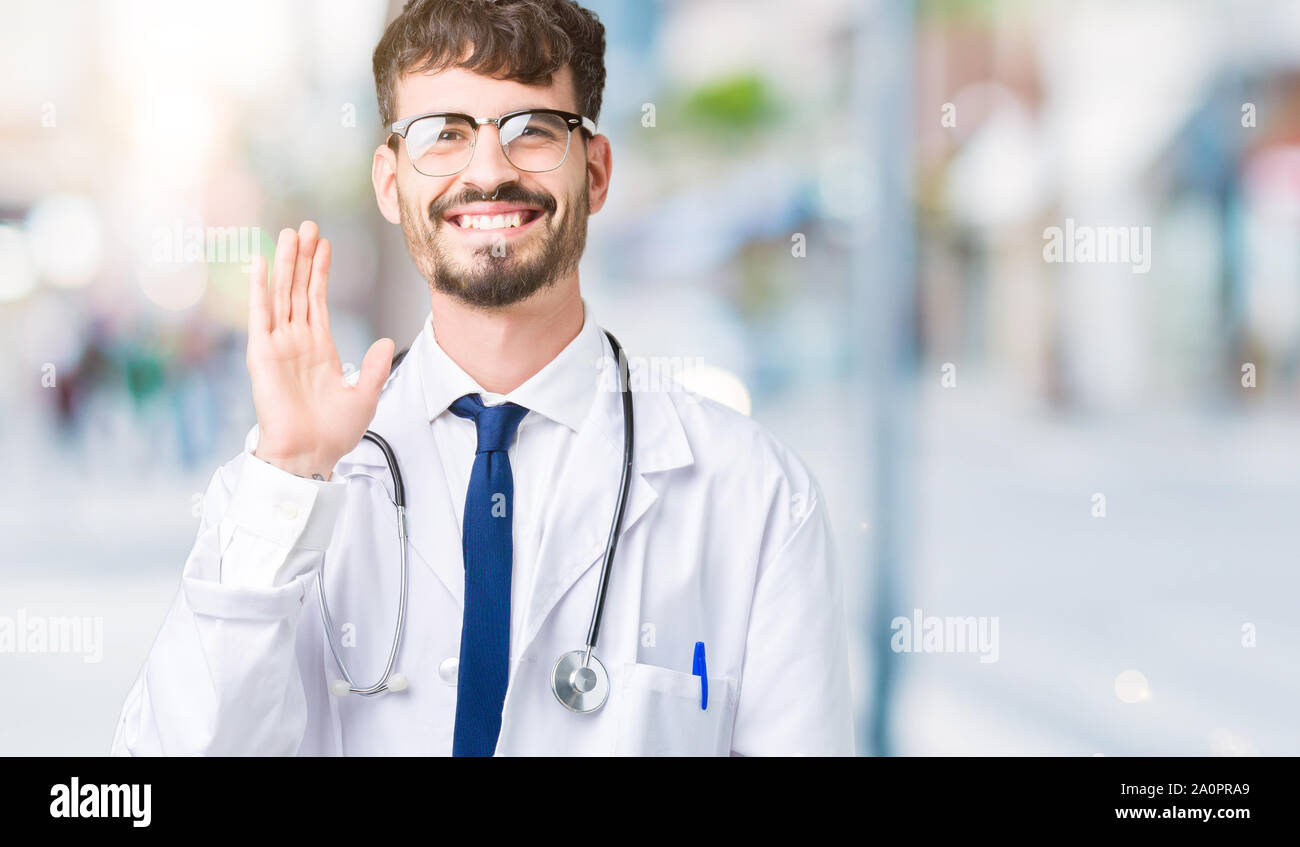 Young doctor man wearing hospital coat over isolated background Waiving ...