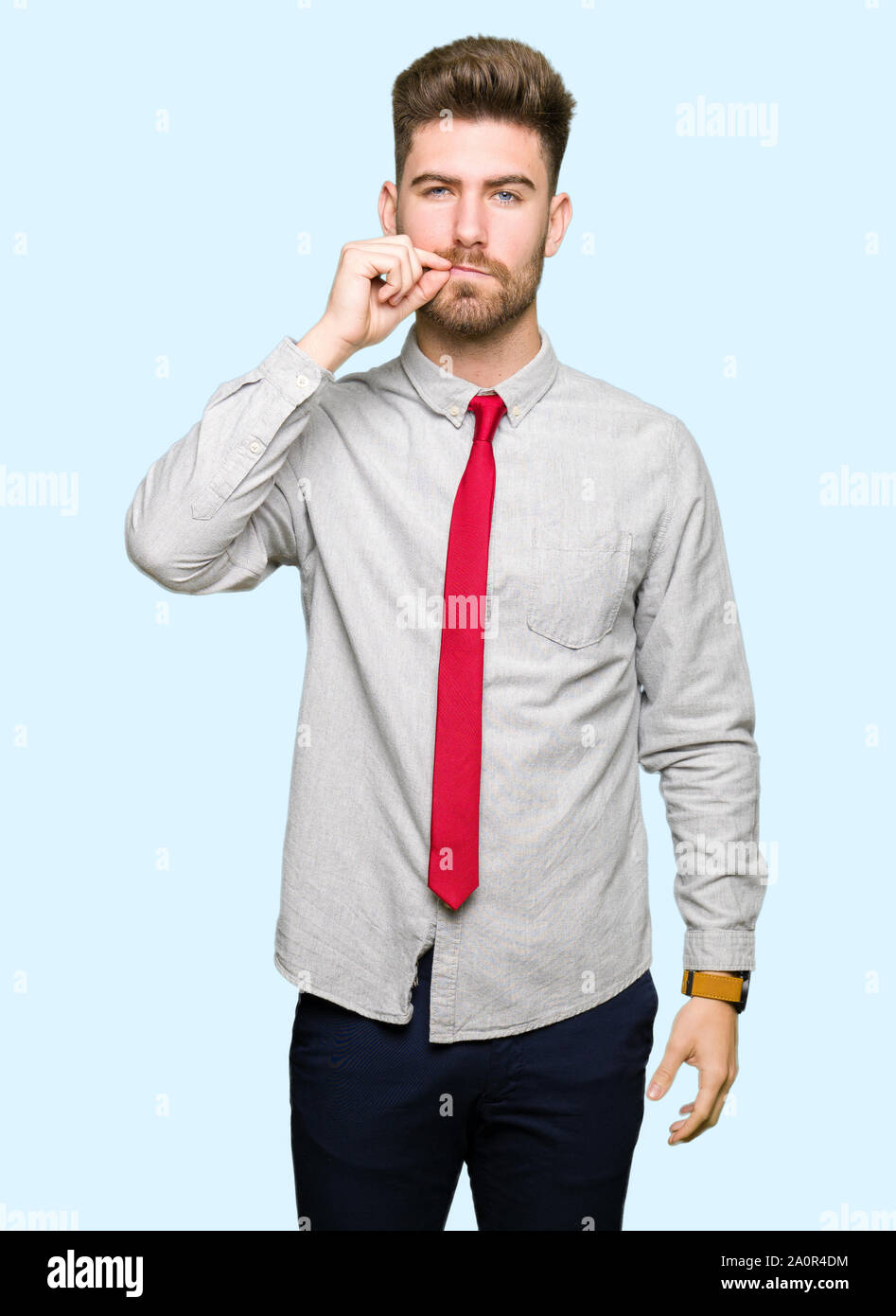 Young handsome business man mouth and lips shut as zip with fingers ...