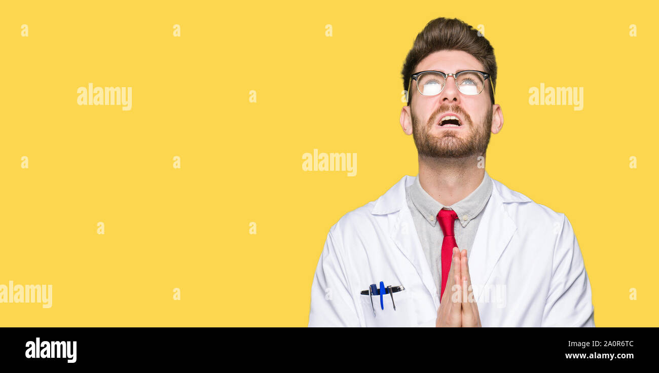 Young handsome scientist man wearing glasses begging and praying with ...