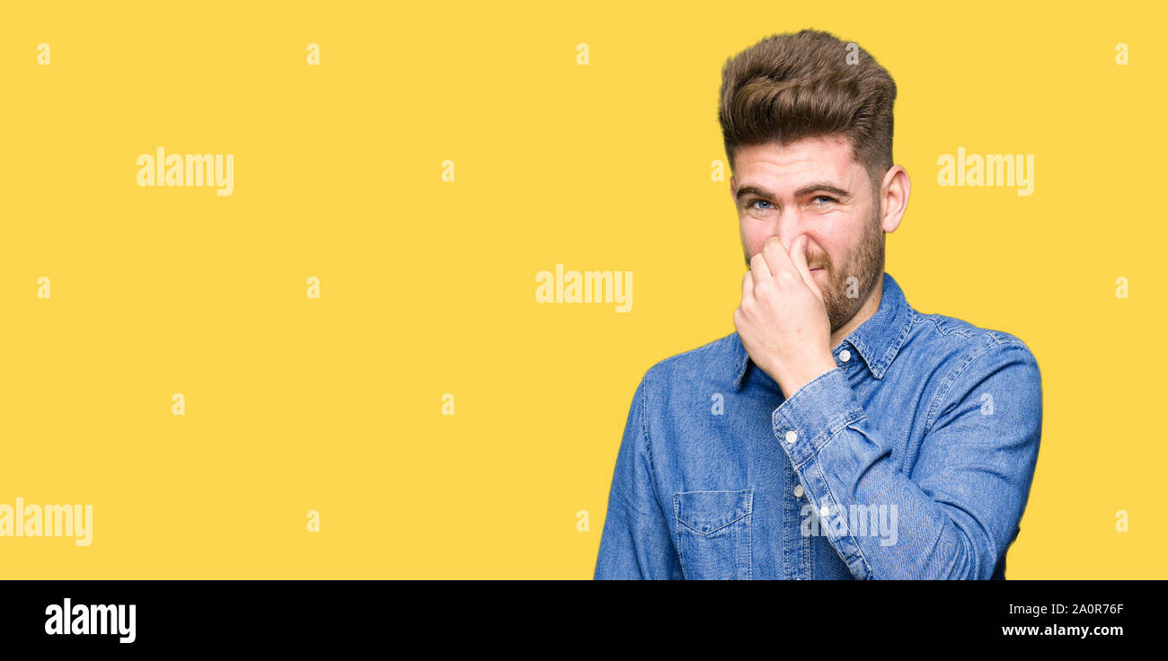 Young handsome blond man wearing casual denim shirt smelling something ...