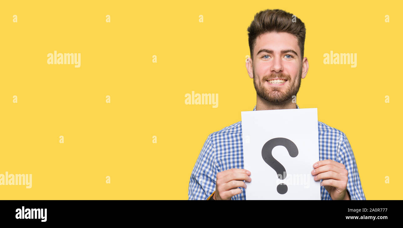 Young handsome man holding paper with question mark with a happy face ...