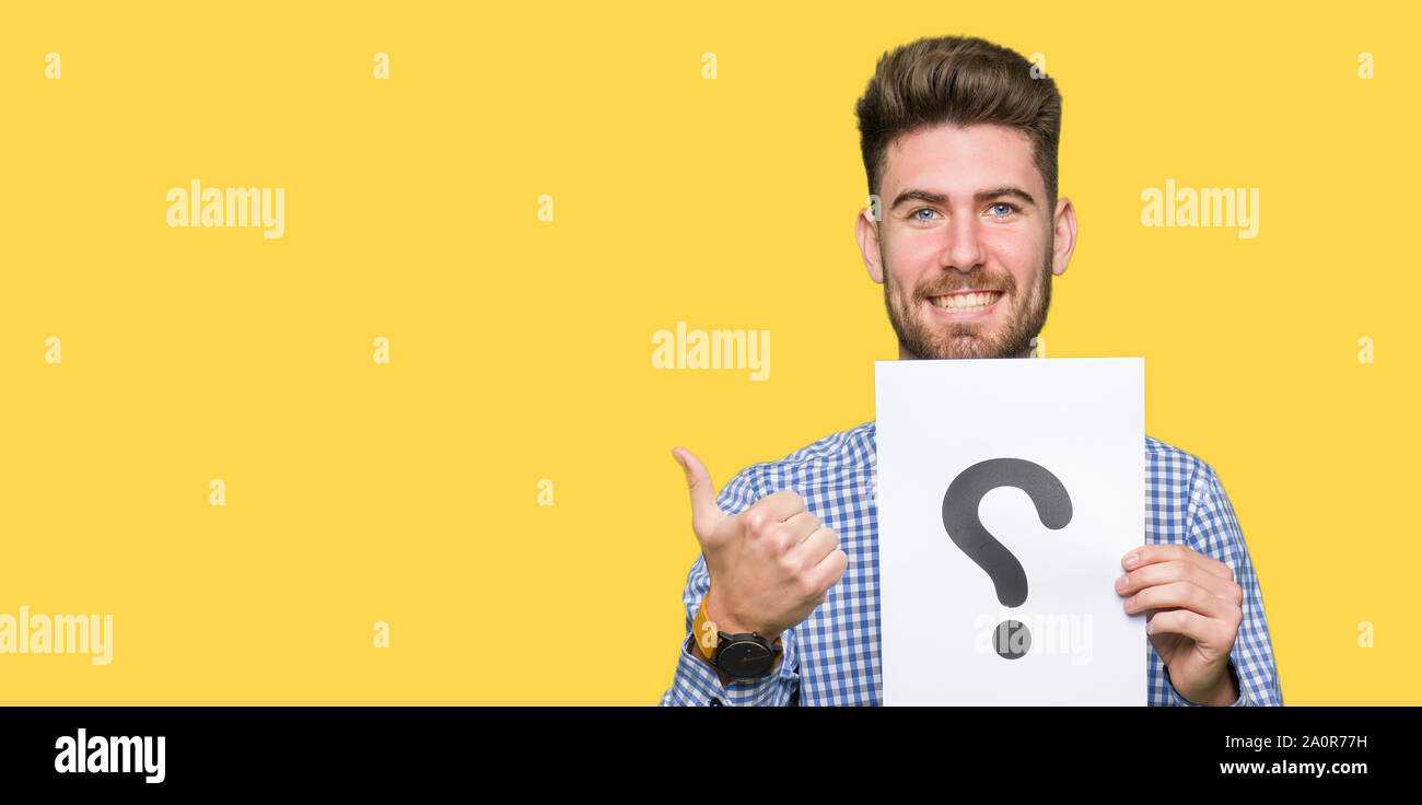 Young handsome man holding paper with question mark happy with big ...