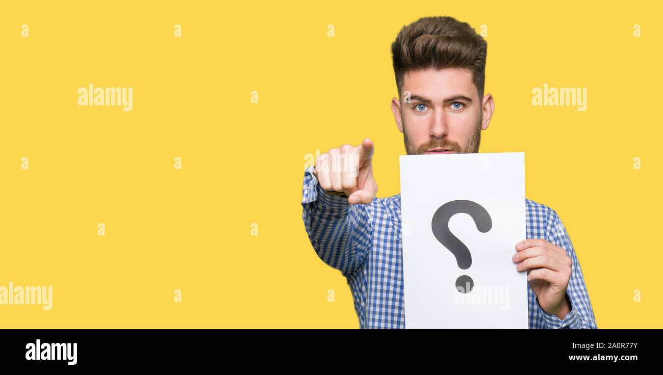 Young handsome man holding paper with question mark pointing with ...