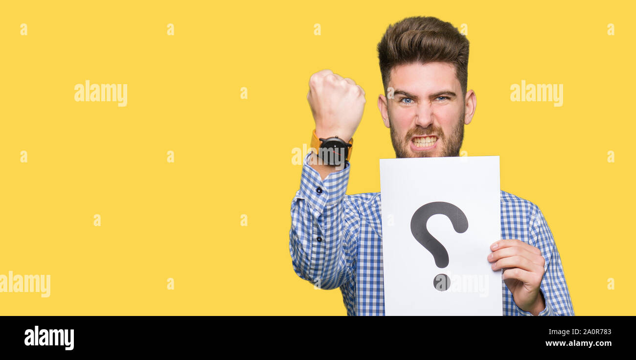 Young handsome man holding paper with question mark annoyed and ...