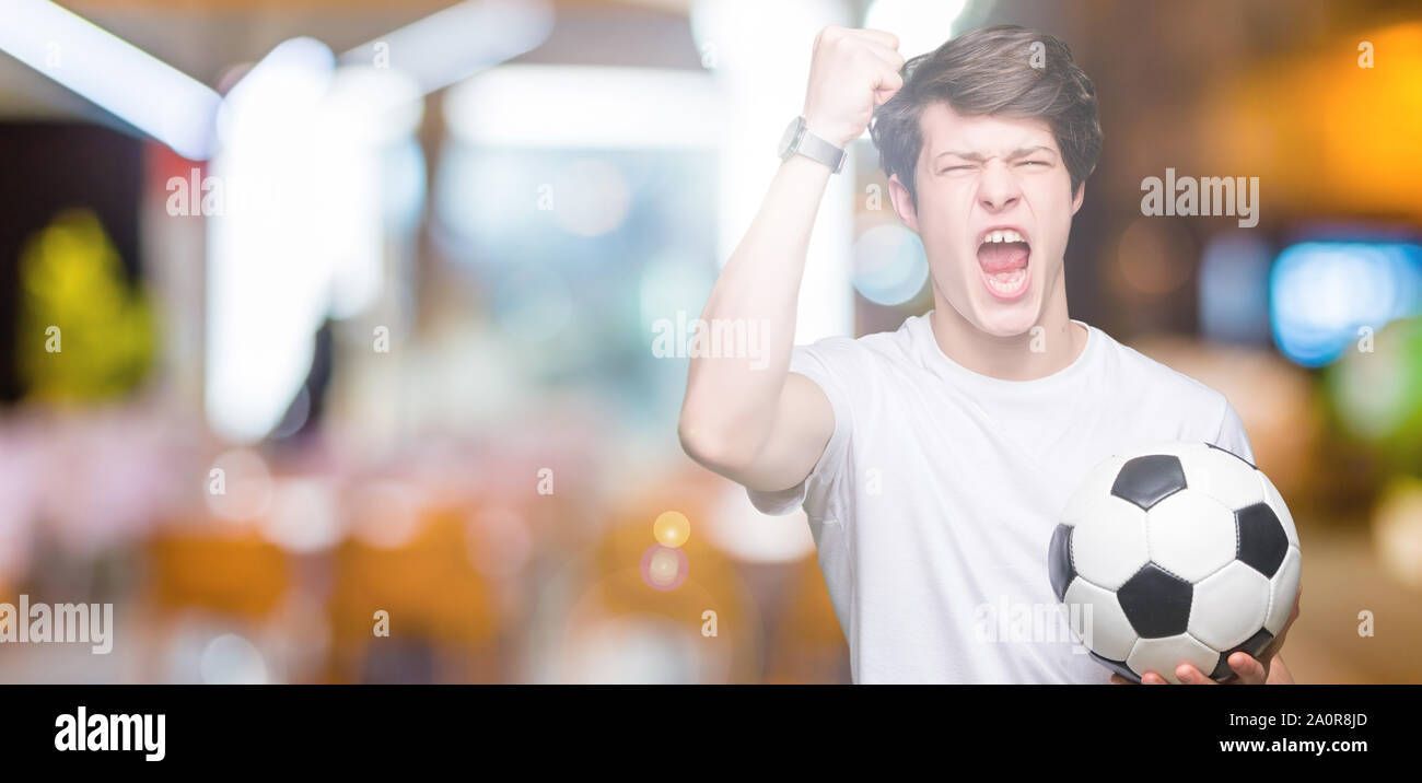 Young man holding soccer football ball over isolated background annoyed ...