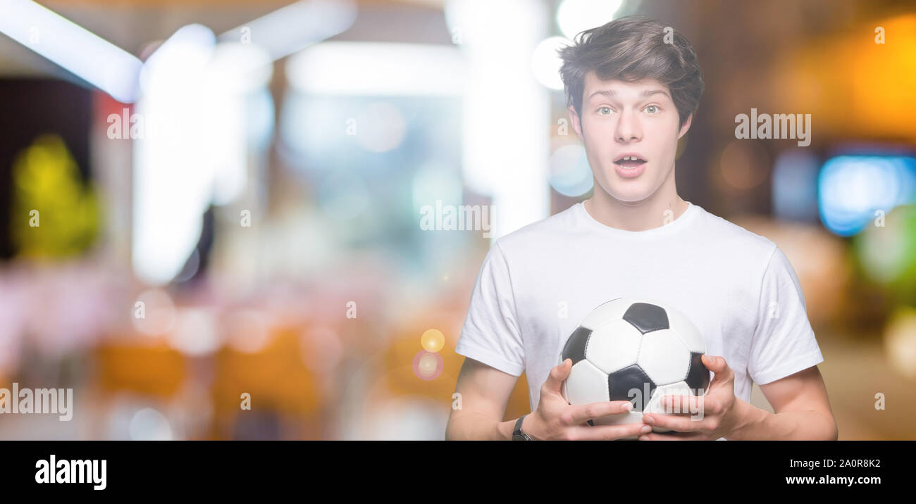 Young man holding soccer football ball over isolated background scared ...