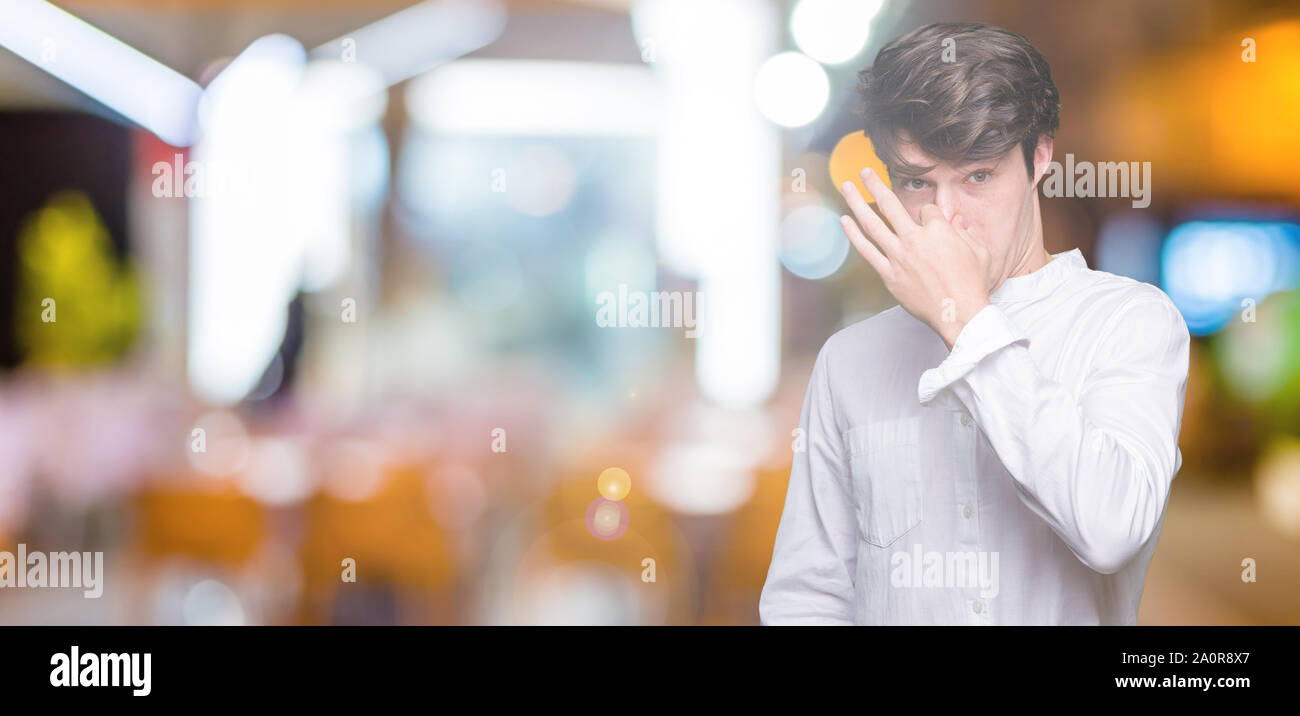 Young handsome business man over isolated background smelling something ...