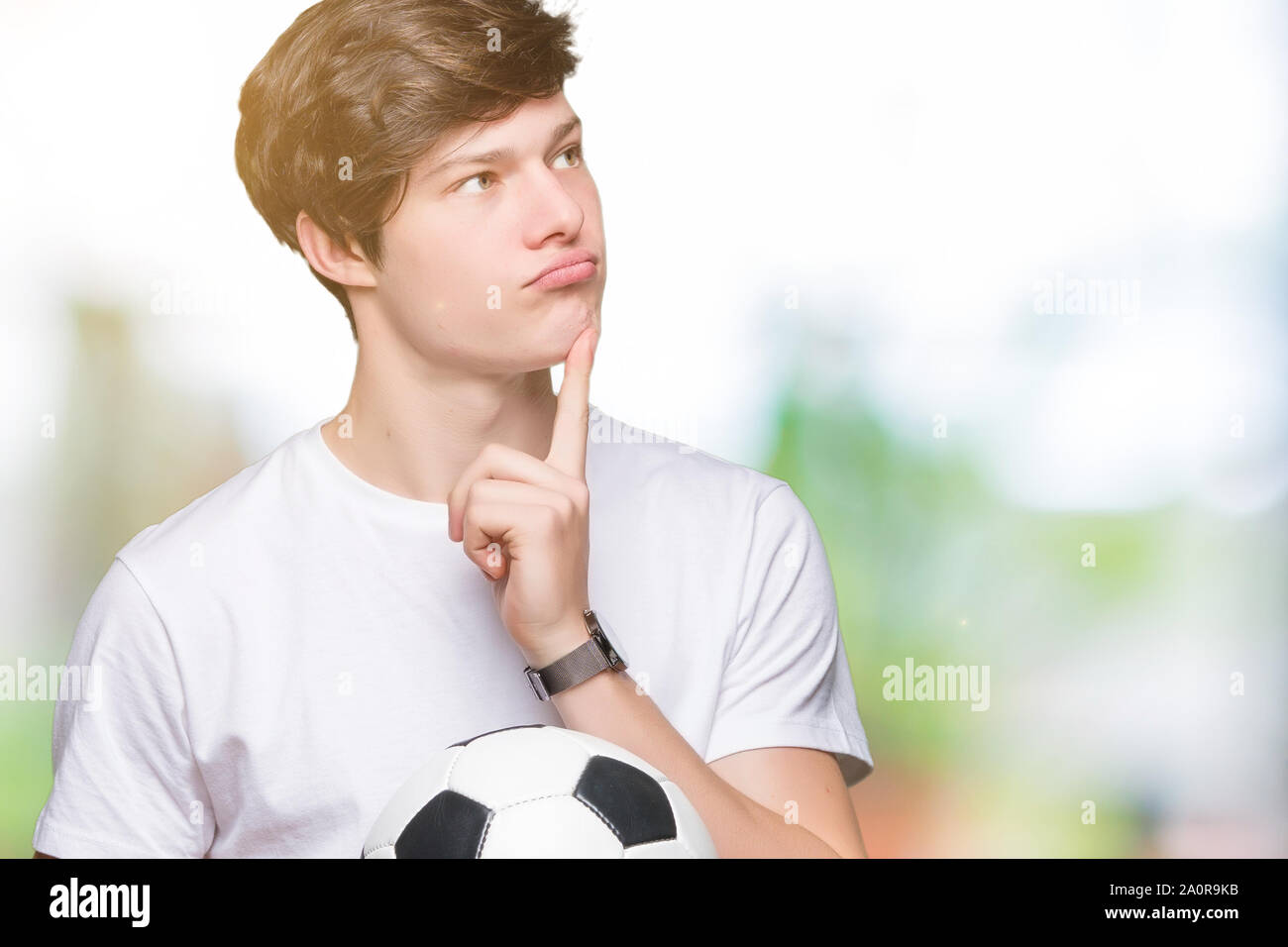 Young man holding soccer football ball over isolated background serious ...