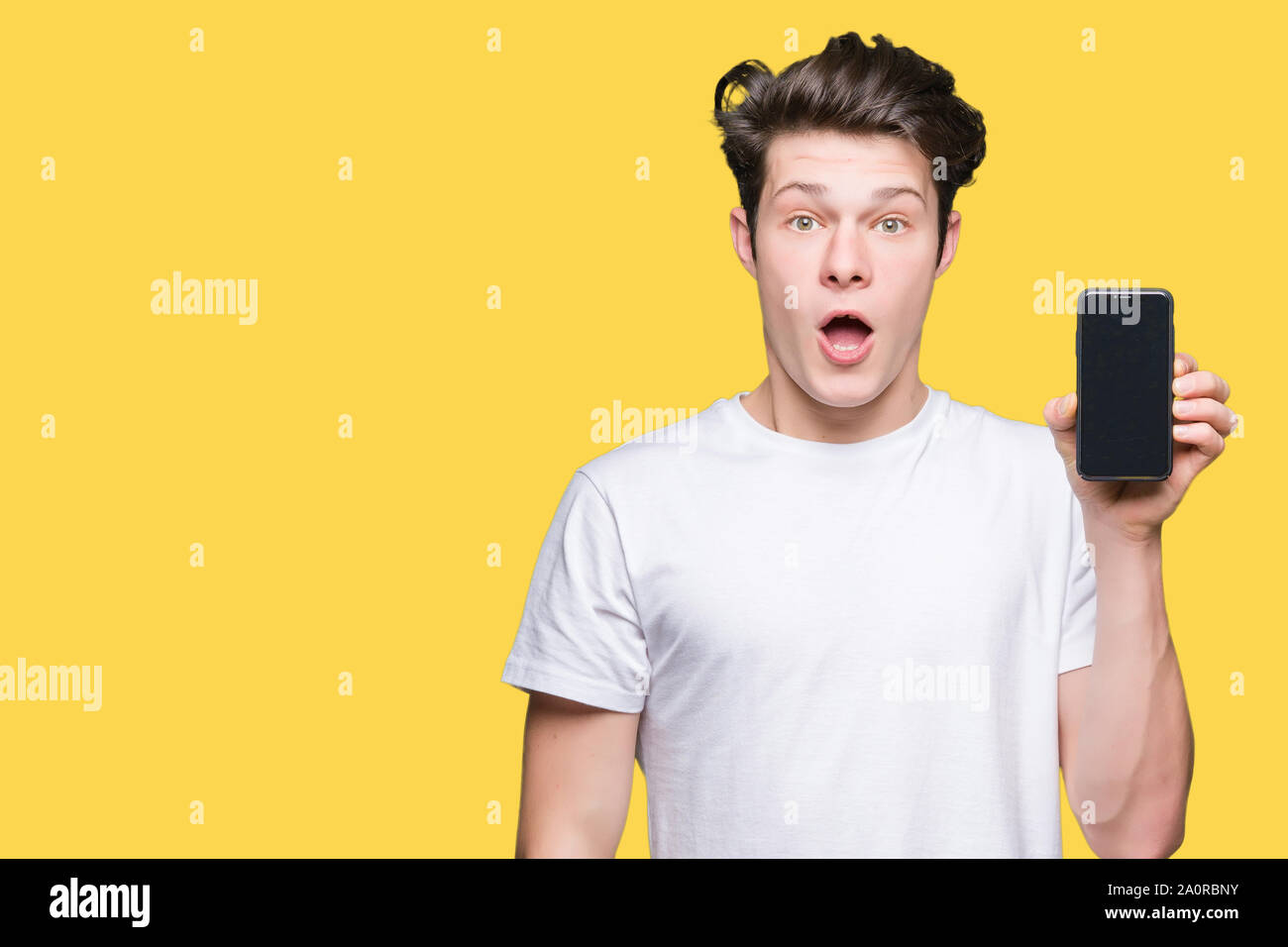 Young man showing smartphone screen over isolated background scared in ...