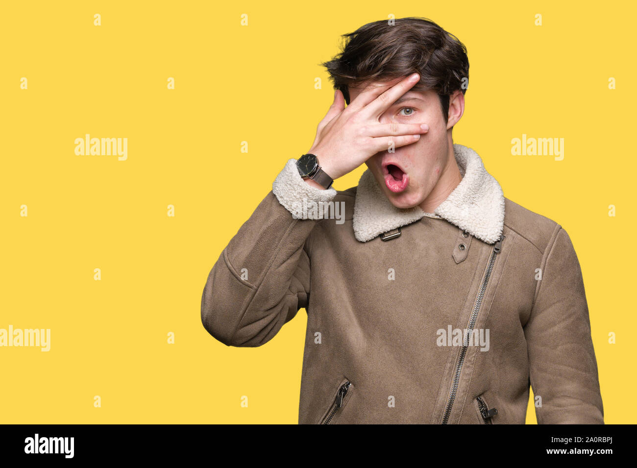 Young handsome man wearing winter coat over isolated background peeking ...