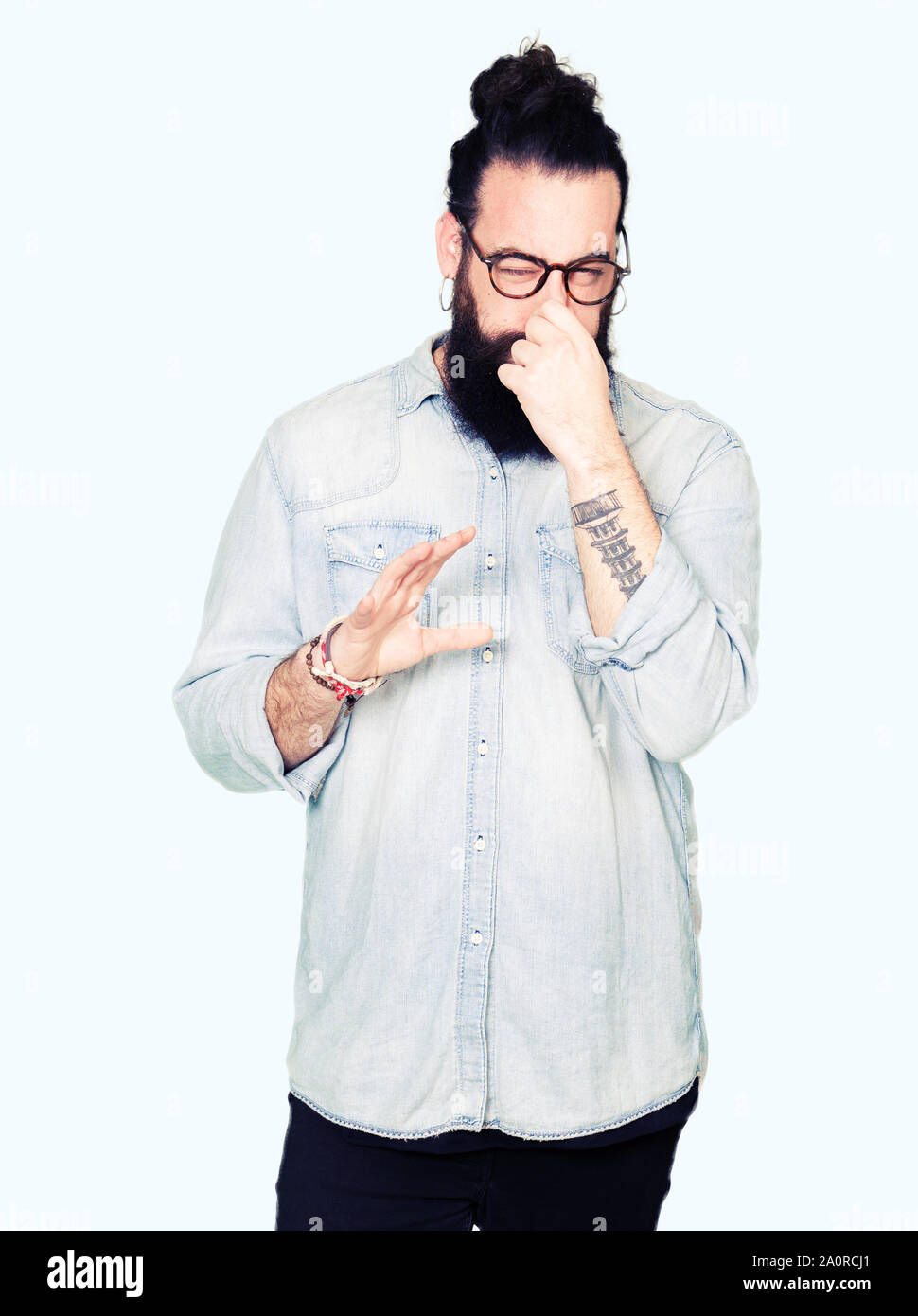 Young hipster man with long hair and beard wearing glasses smelling ...