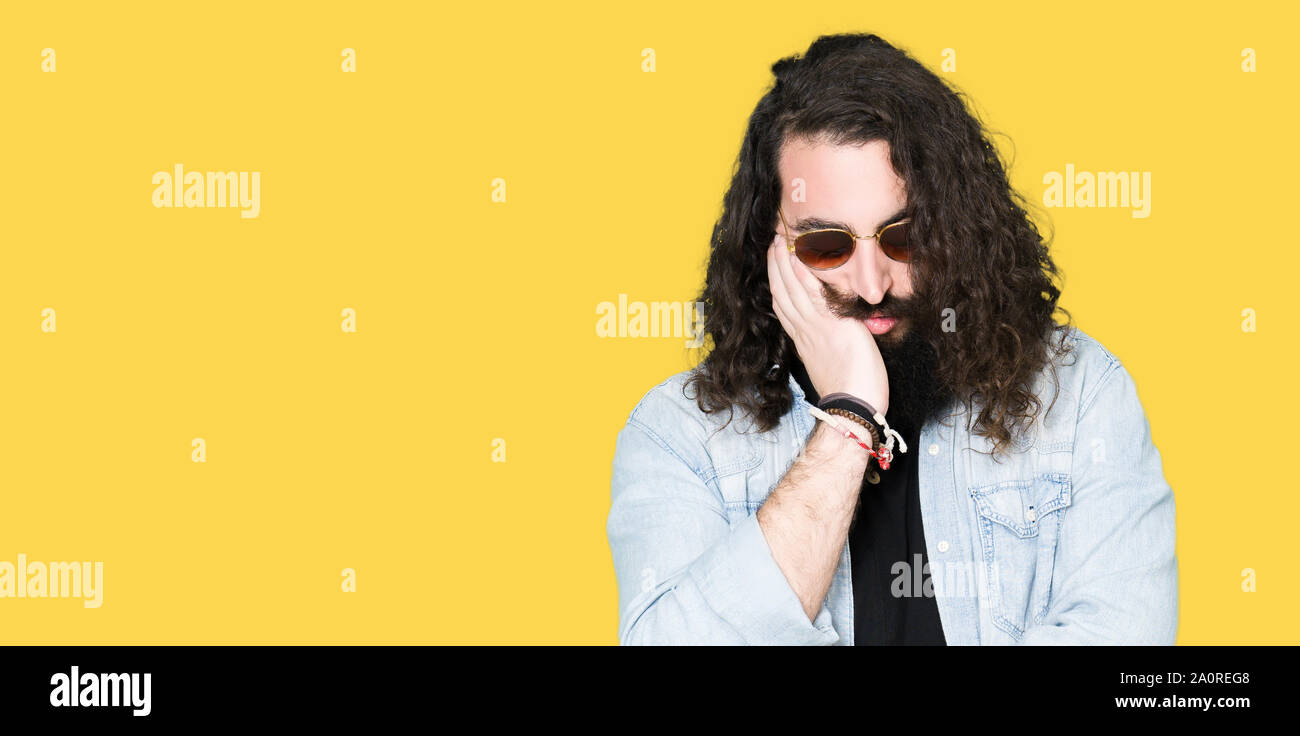 Young hipster man with long hair and beard wearing sunglasses thinking ...