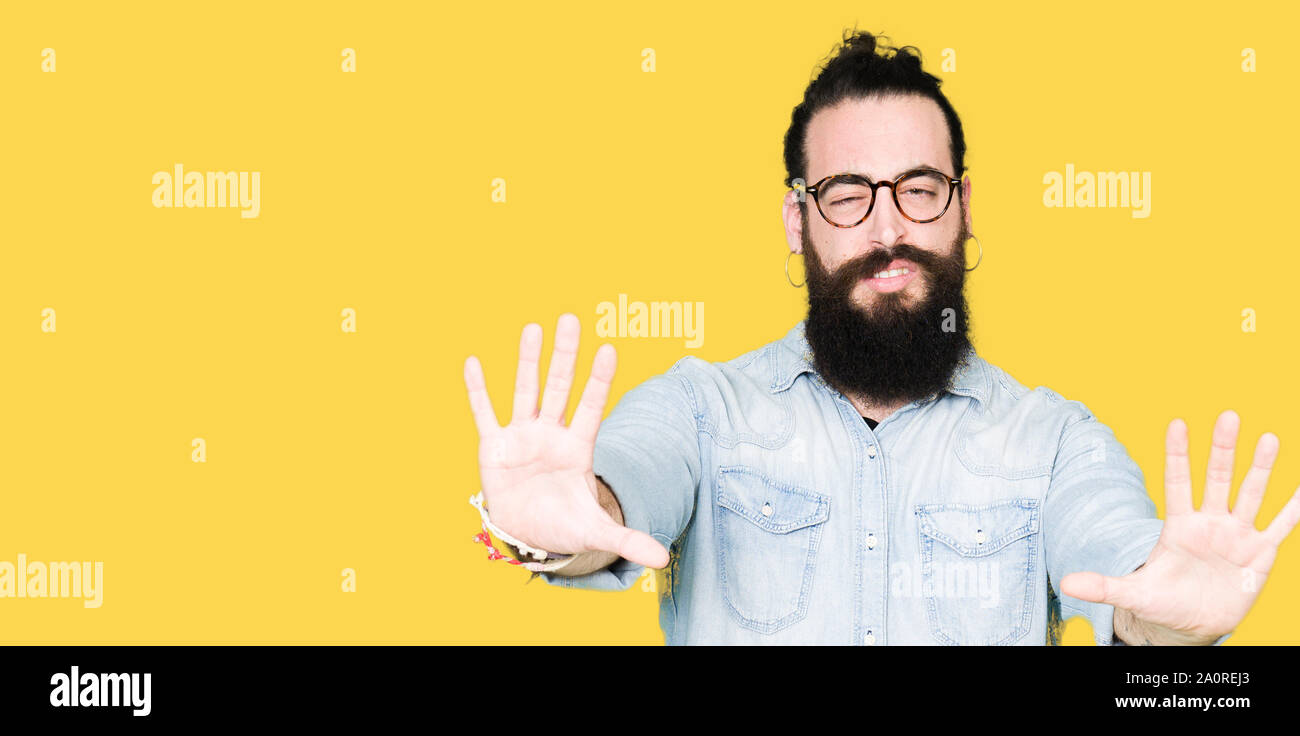 Young hipster man with long hair and beard wearing glasses afraid and ...